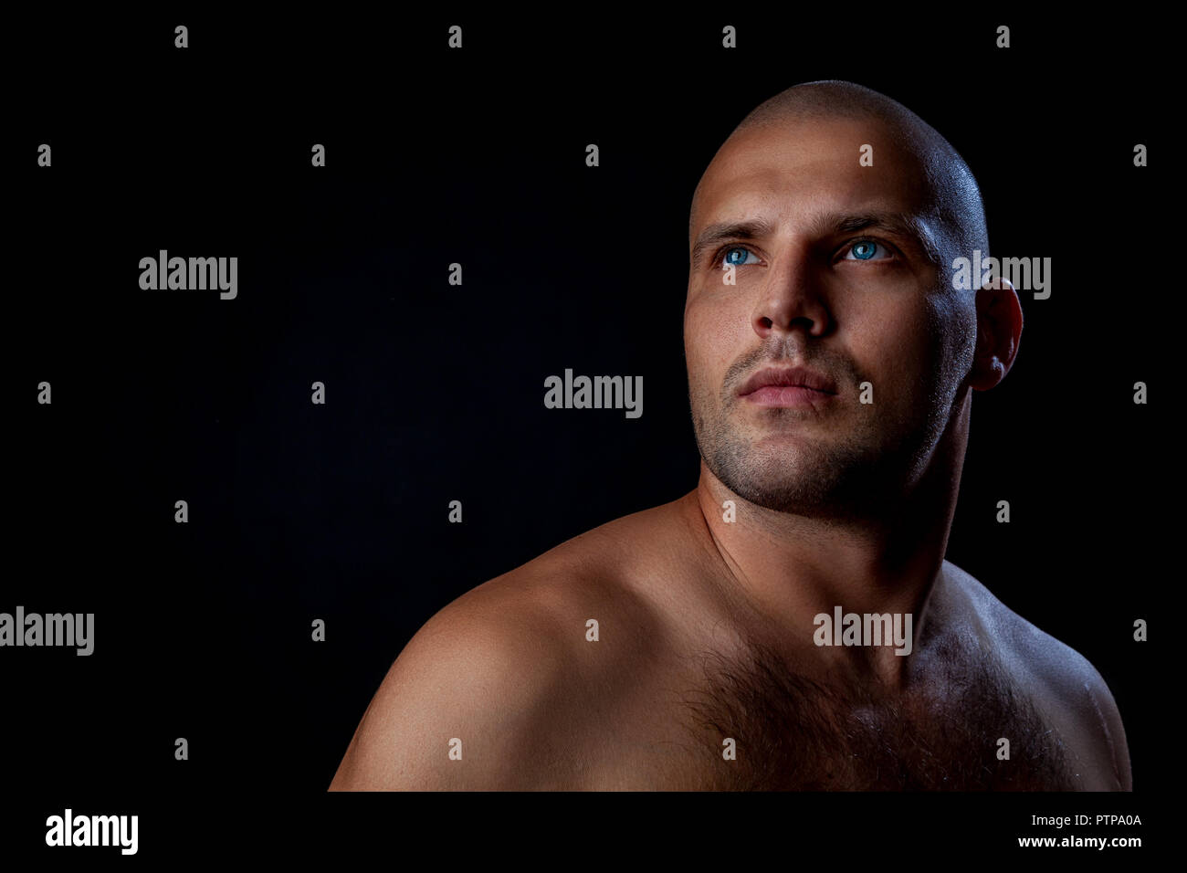 Serious young bald man standing isolated on a black background and ...