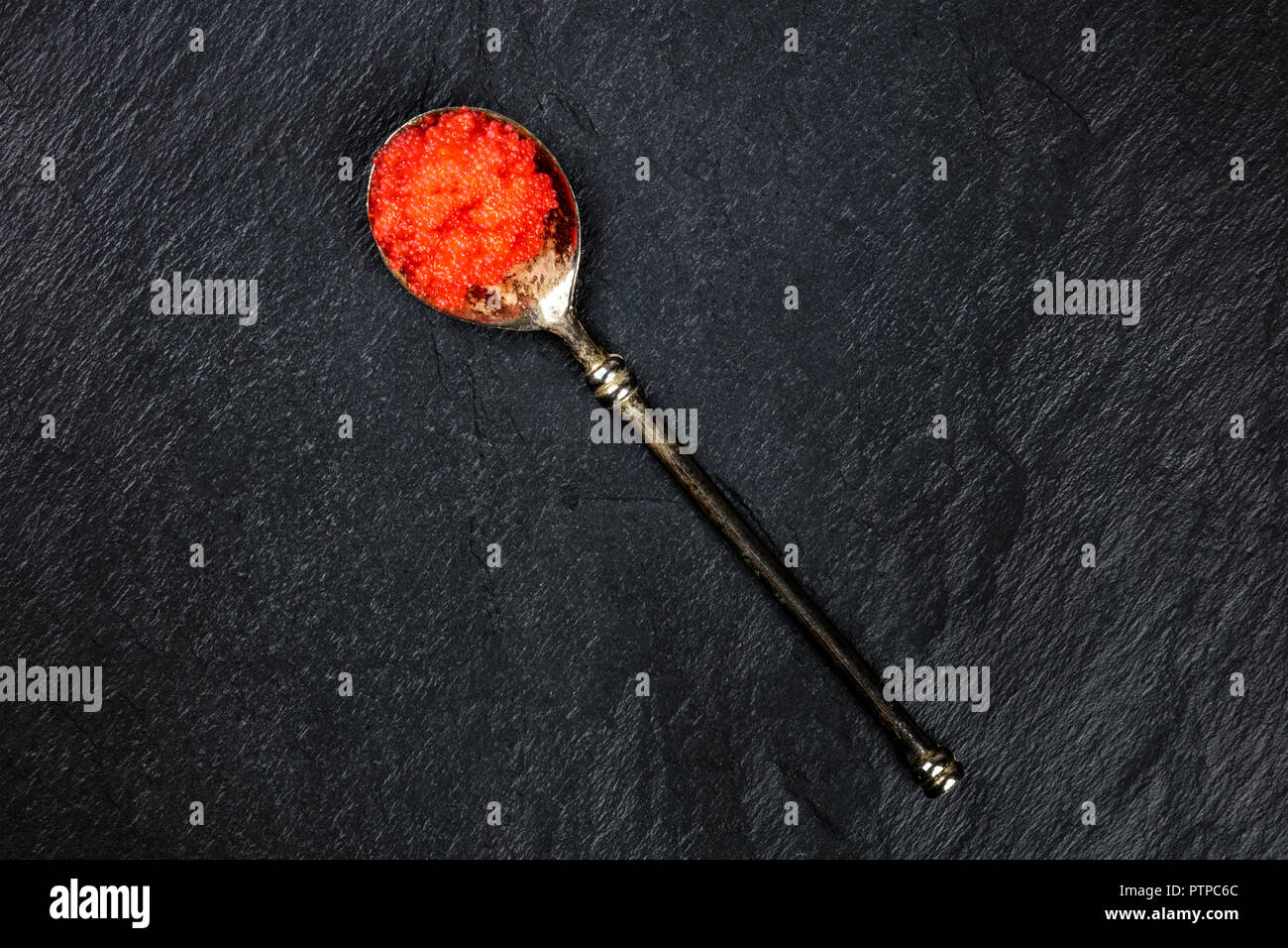An overhead photo of red caviar in a spoon, shot from above on a black ...