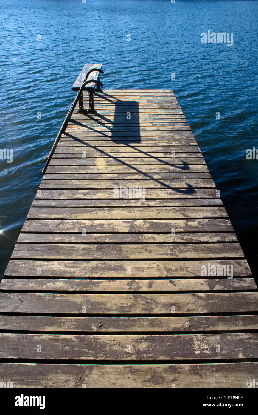 Beautiful wooden pier with bench and sun reflected on calm and blue ...