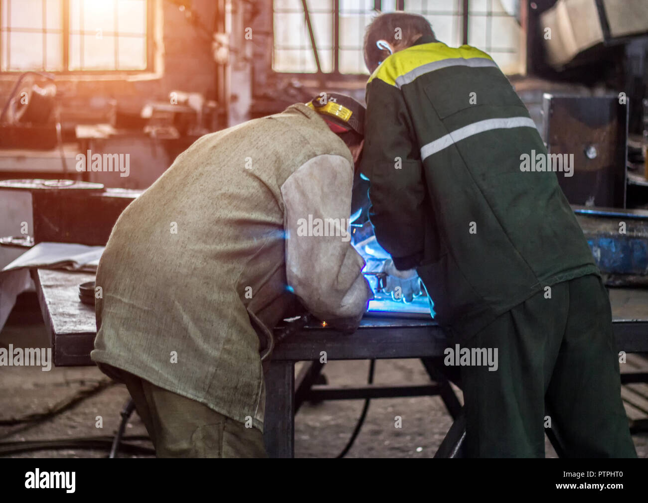 Two male workers at the factory welder and his assistant weld parts ...