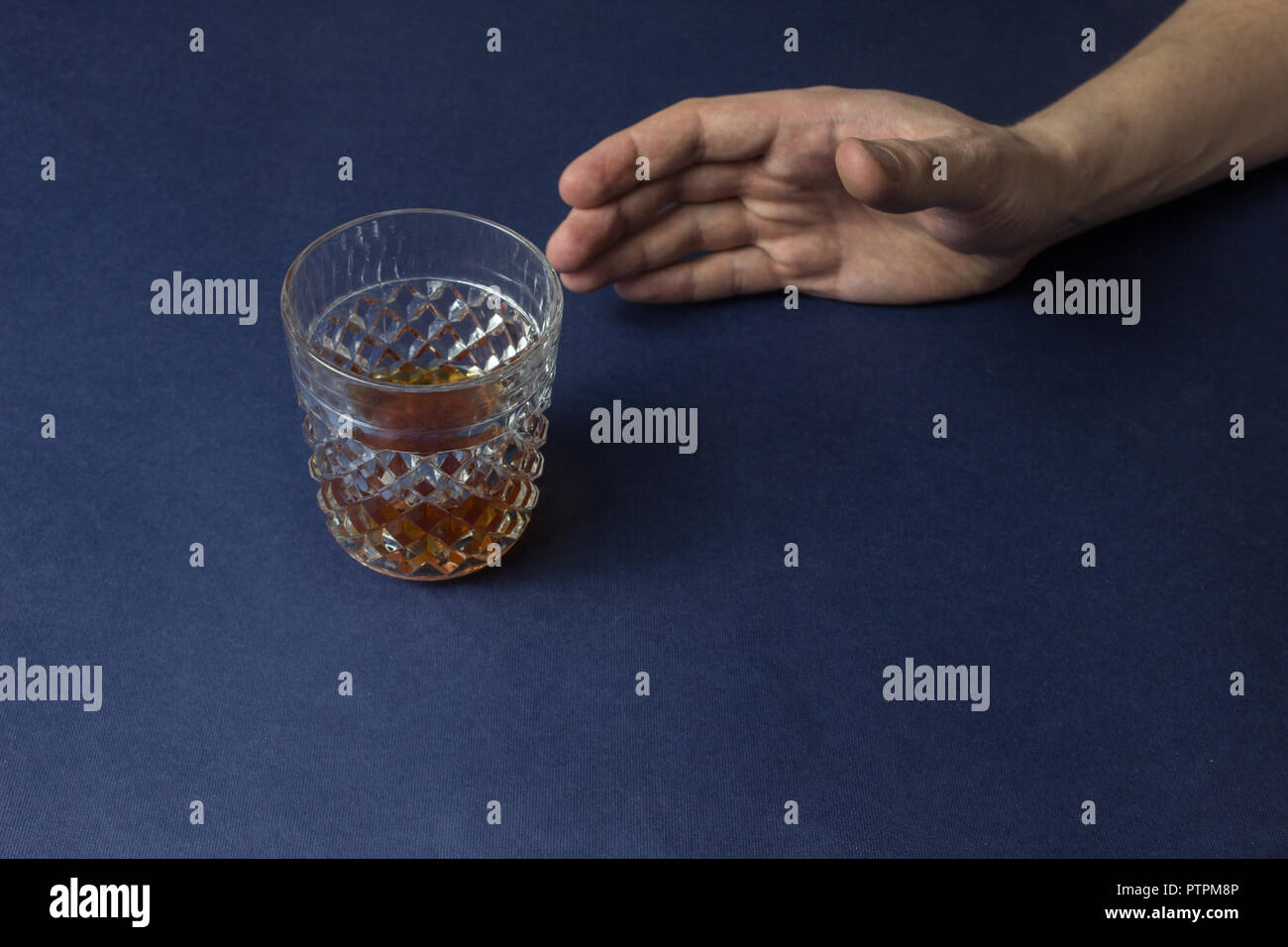 Male hand reaching for a glass with alcohol, close-up, blue background ...