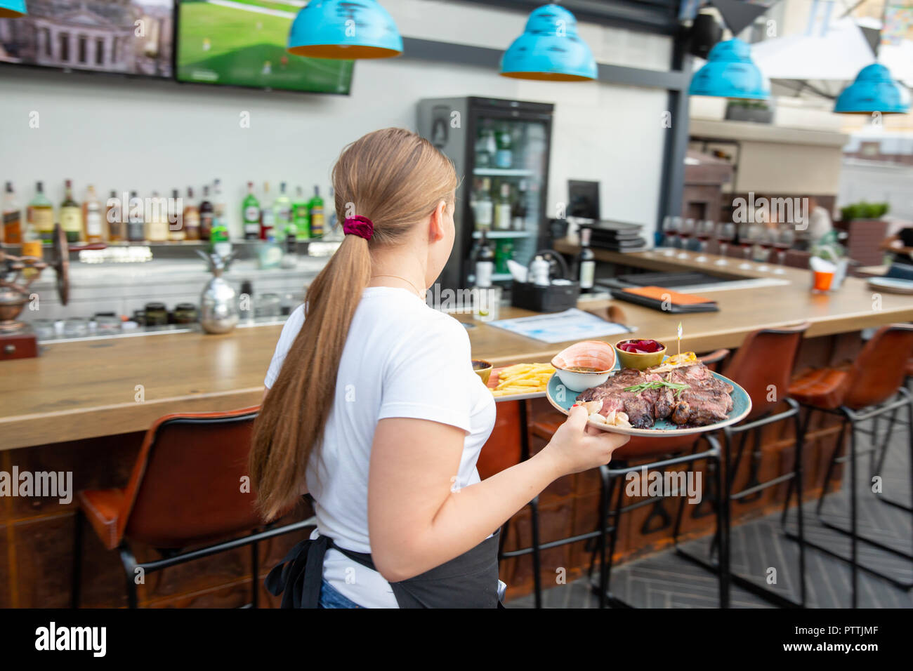 Waitress is carrying a plate with meat dish at the outdoor restaurant ...