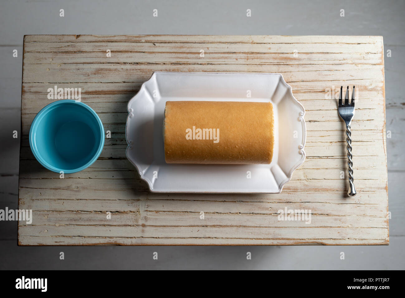 Arctic roll cake on a plate next to a colourful bowl and a fork on a ...