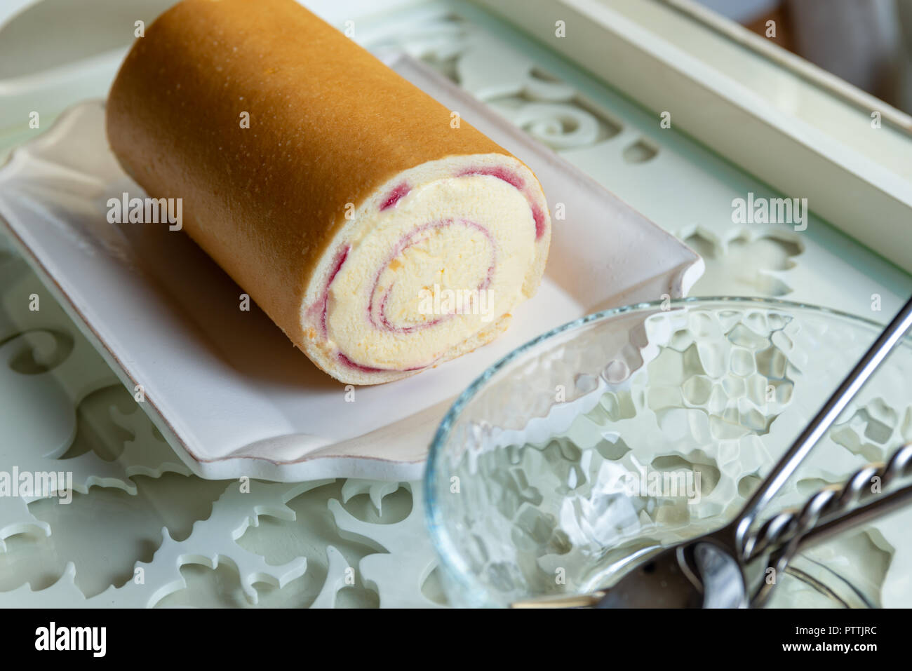 Arctic roll cake on a plate on a tray next to a glass bowl with spoons ...