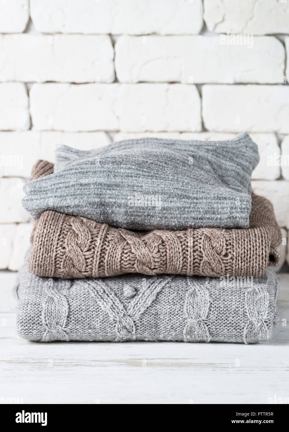 Stack of cozy woolen clothes. Knitted sweters on the table on white ...