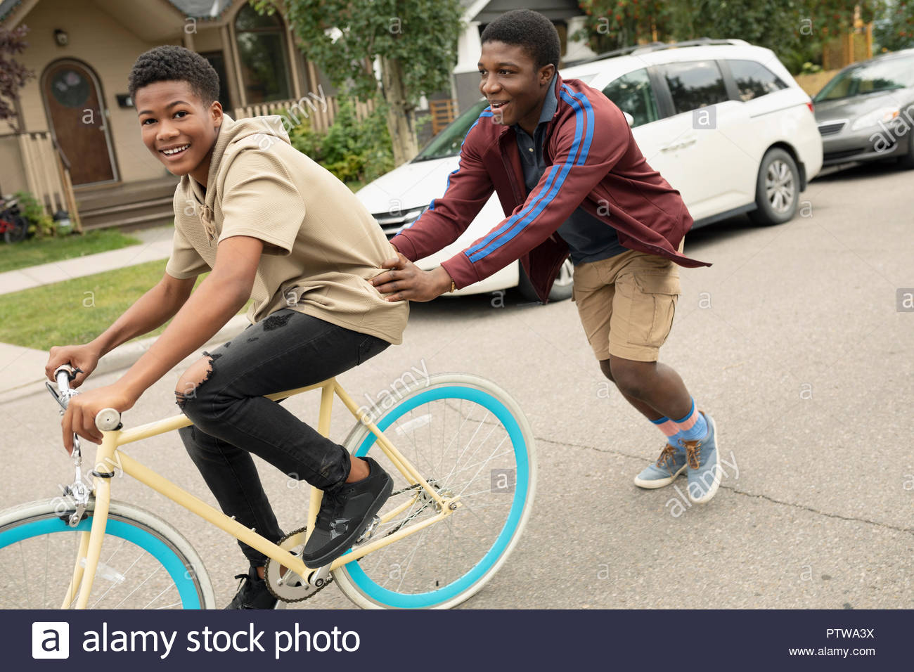Playful teenage boy pushing friend on bicycle on street Stock Photo - Alamy
