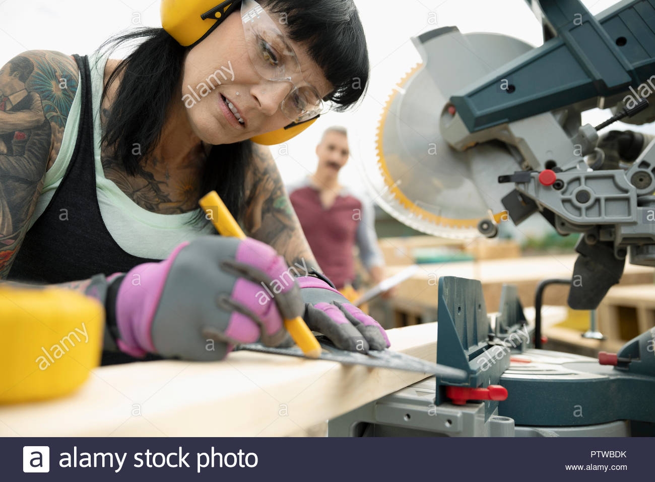 Close up woman with tattoos marking wood, using saw at construction ...