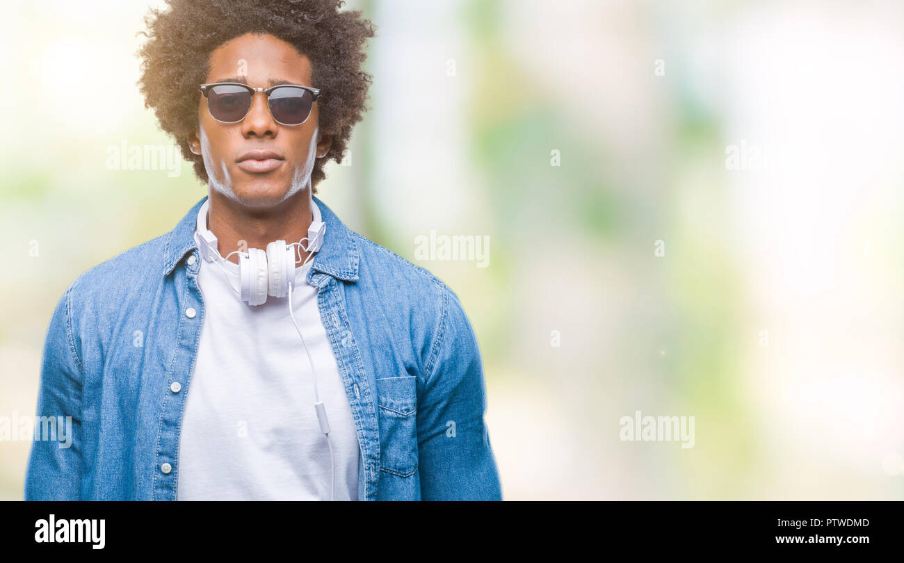 Afro american man wearing headphones listening to music over isolated background with serious ...