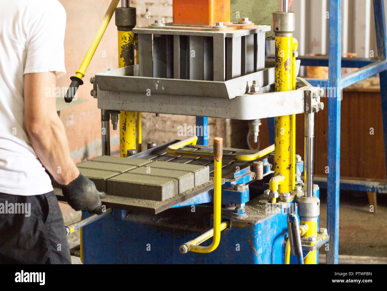 The worker makes a sidewalk tile behind the machine, a close-up, paving ...