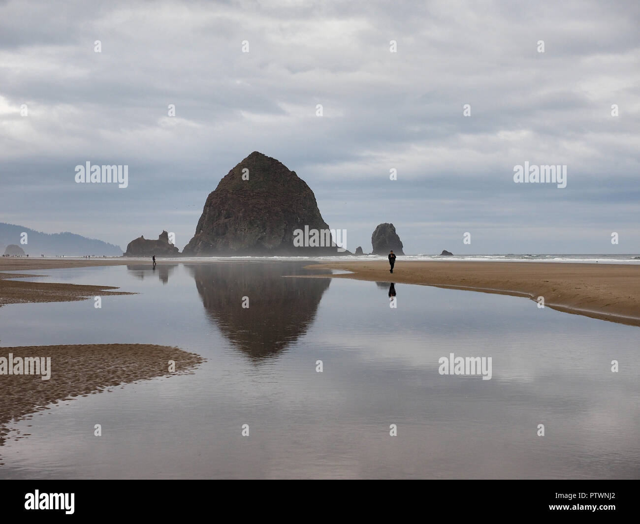 Man photographing Haystack Rock and its reflection on Cannon Beach ...