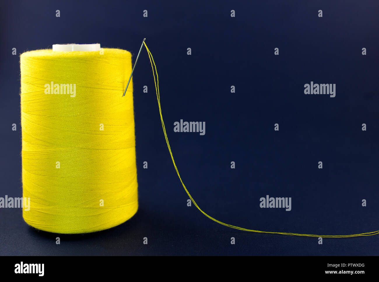 Yellow skein of thread with a needle on a blue background Stock Photo - Alamy