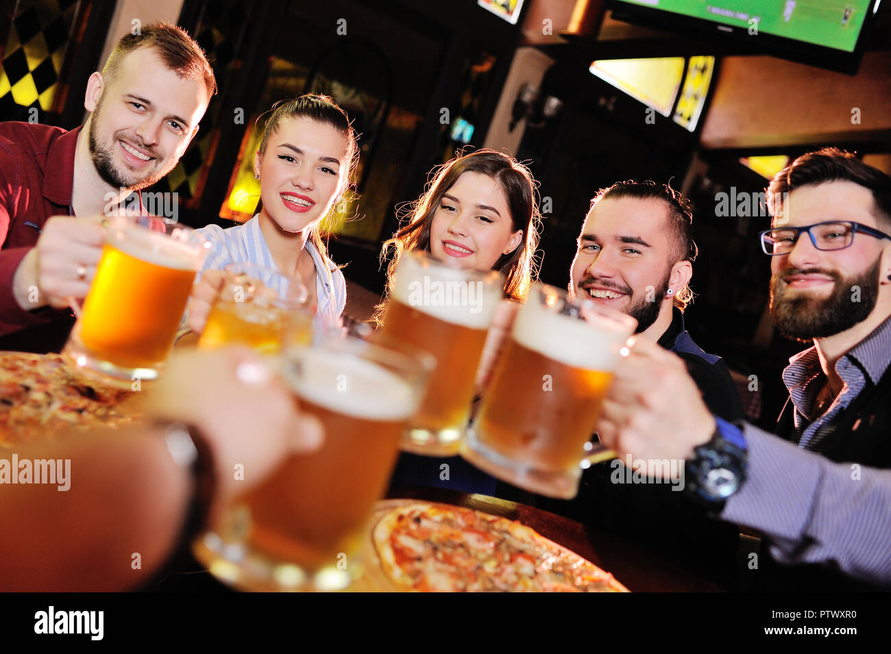 happy cheerful friends drink draft beer and clink glasses in a bar or ...