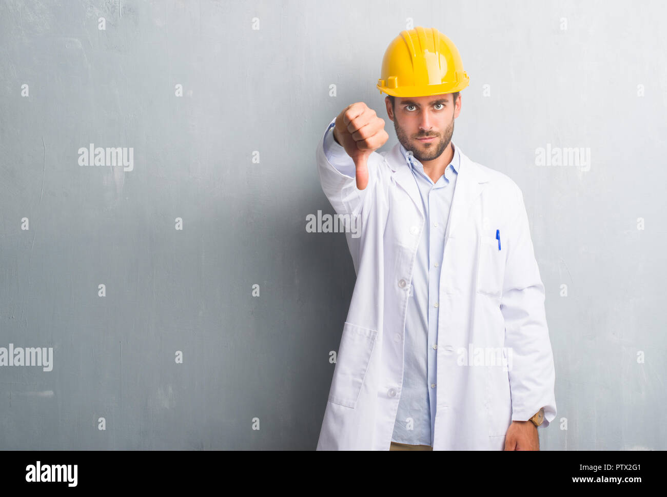 Handsome young engineer man over grey grunge wall wearing safety helmet ...