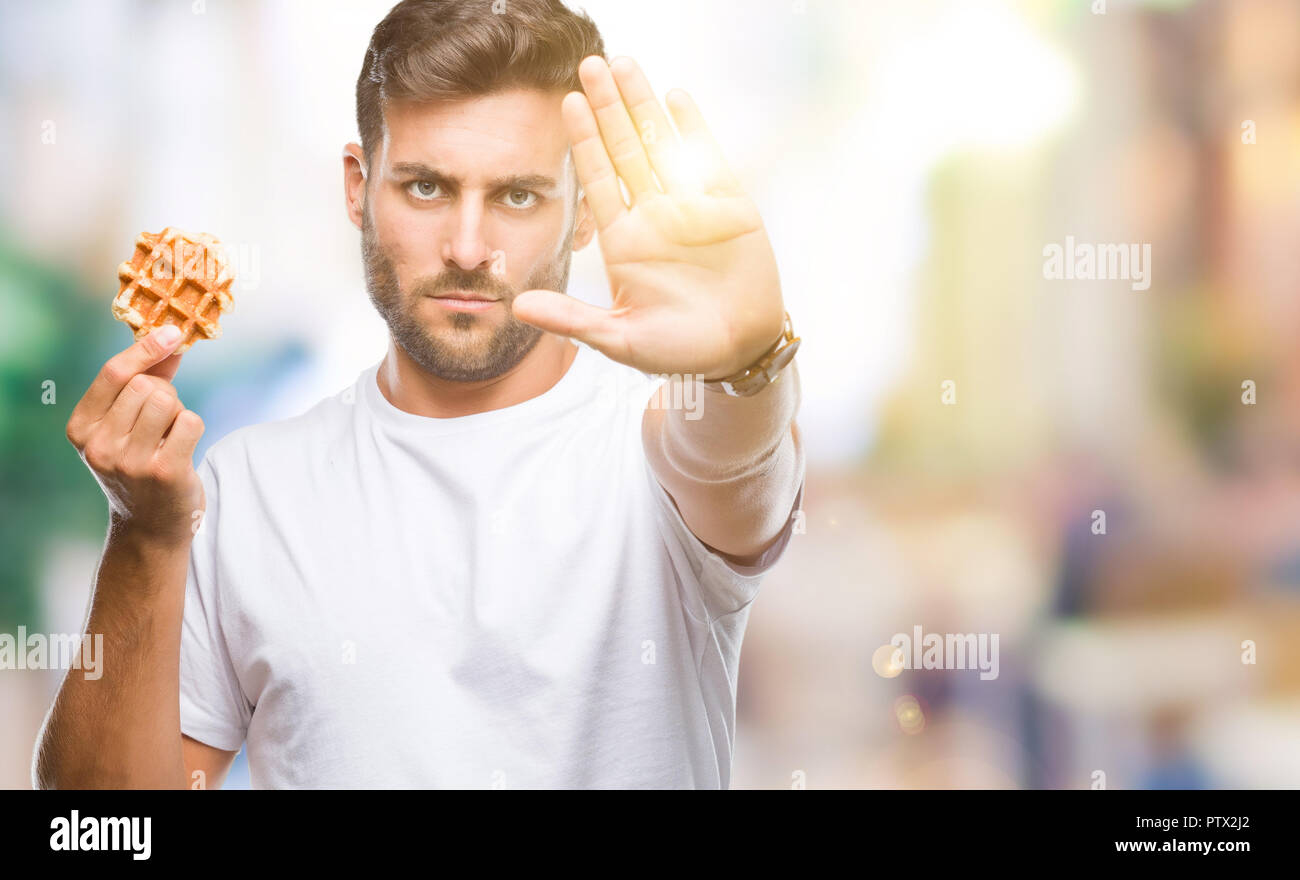 Young handsome man eating a sweet waffle over isolated background with ...
