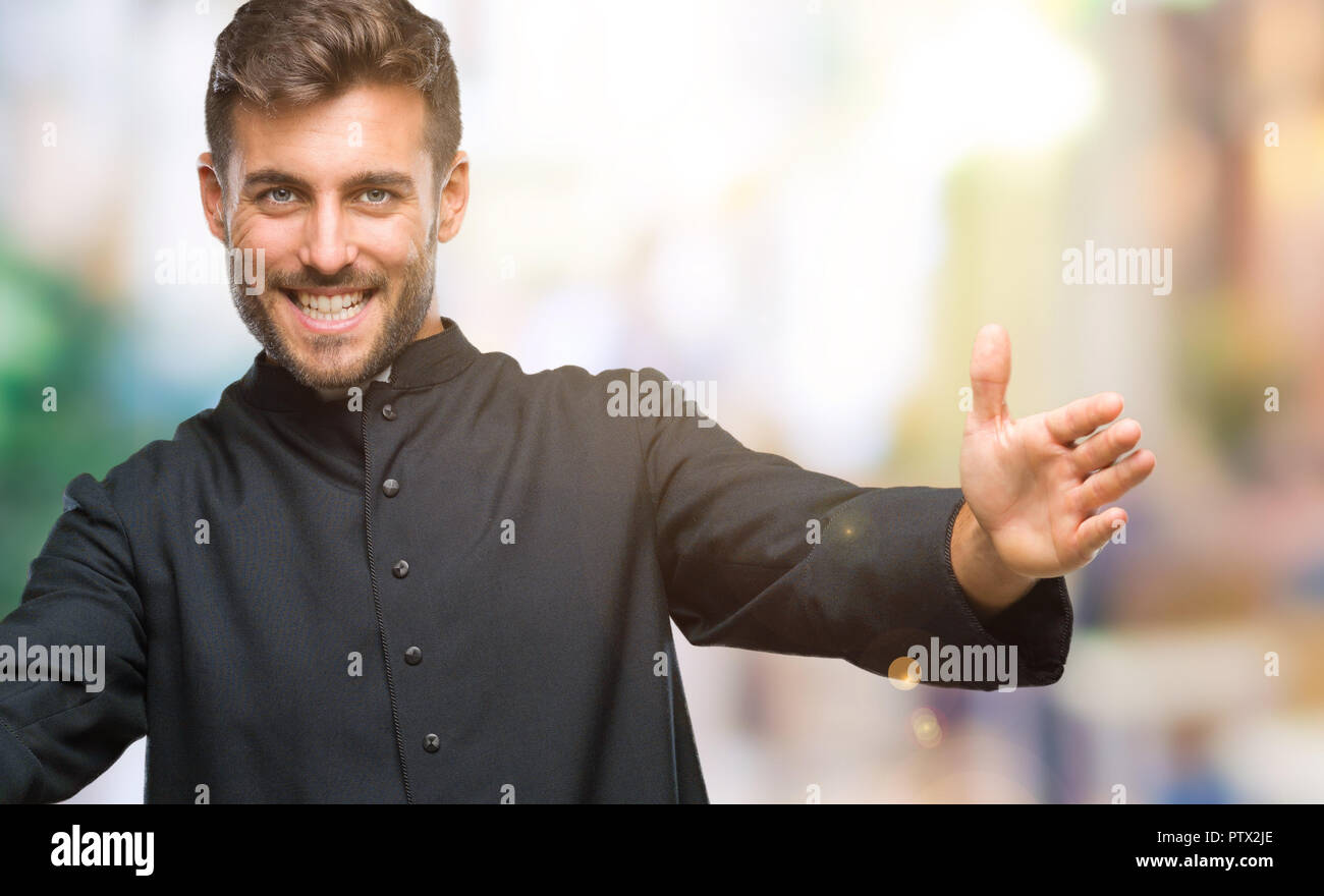Young catholic christian priest man over isolated background looking at ...