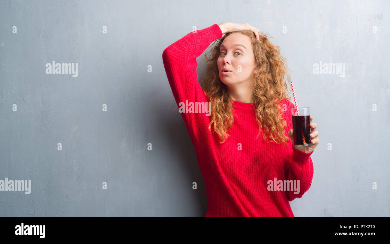 Young redhead woman over grey grunge wall drinking soda refreshment ...