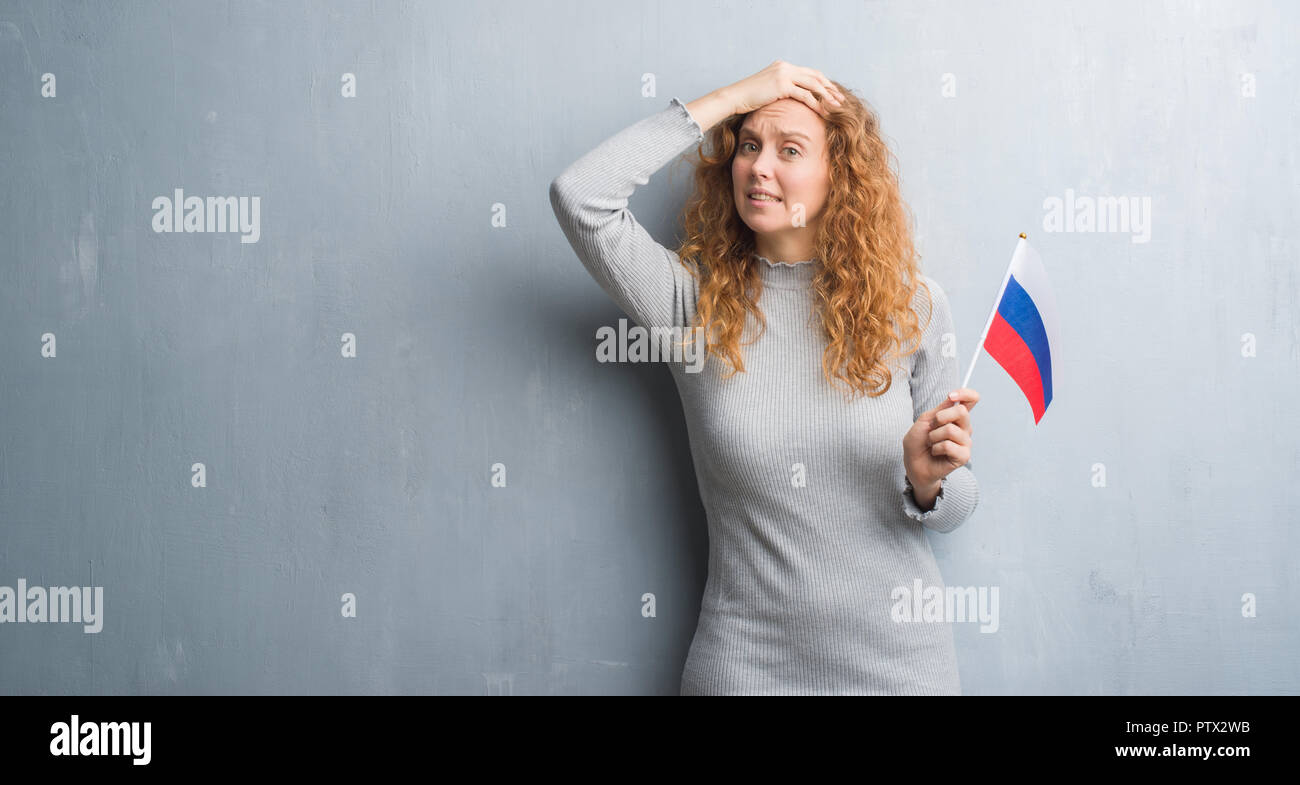 Young redhead woman over grey grunge wall holding flag of Russia ...