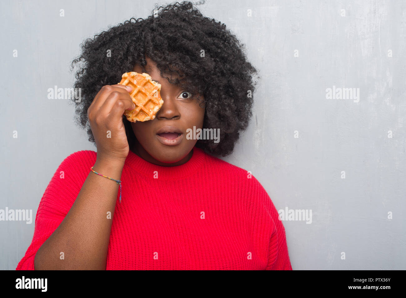 Young african american woman over grey grunge wall eating belgium ...