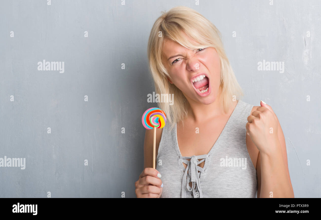 Caucasian adult woman over grey grunge wall eating candy lollipop ...