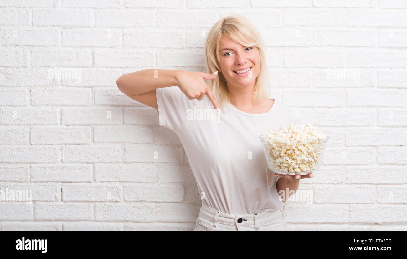 Adult caucasian woman over white brick wall eating pop corn with ...