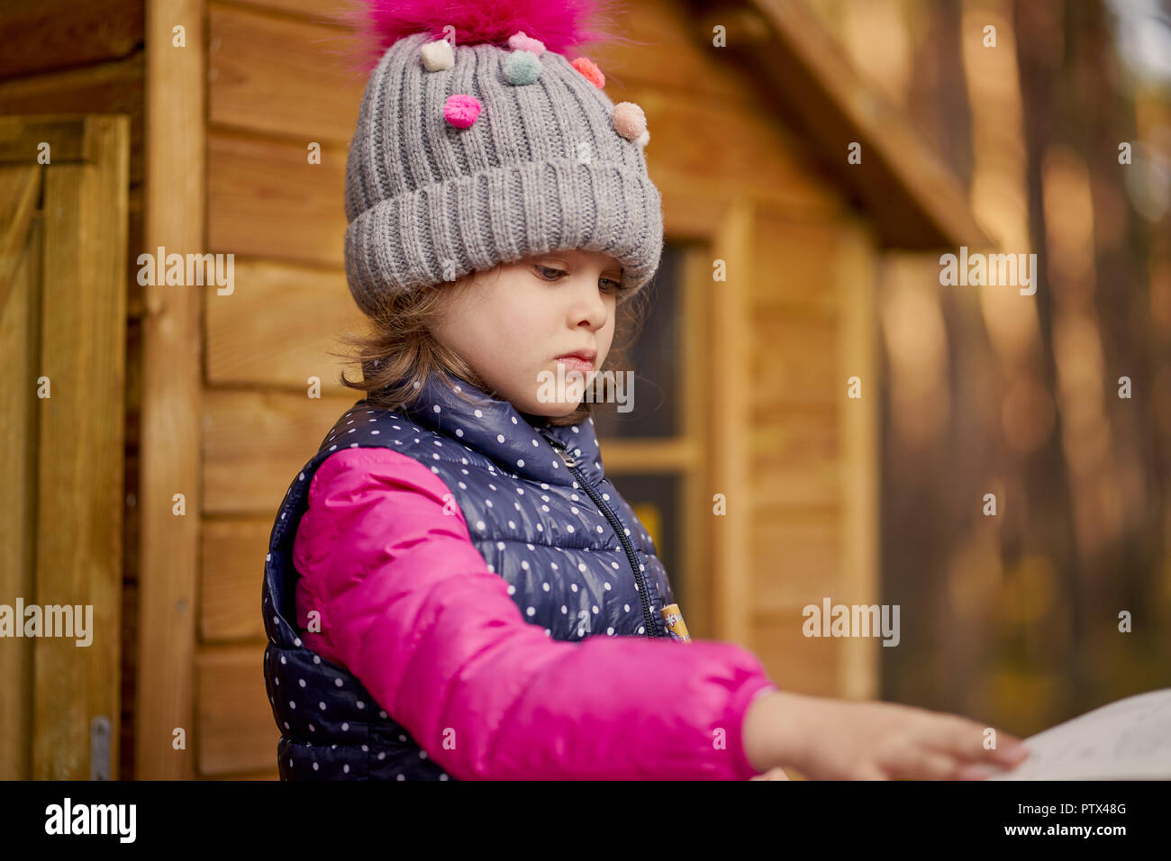 pretty little girl in a hat and jacket is playing on a treehouse in an ...