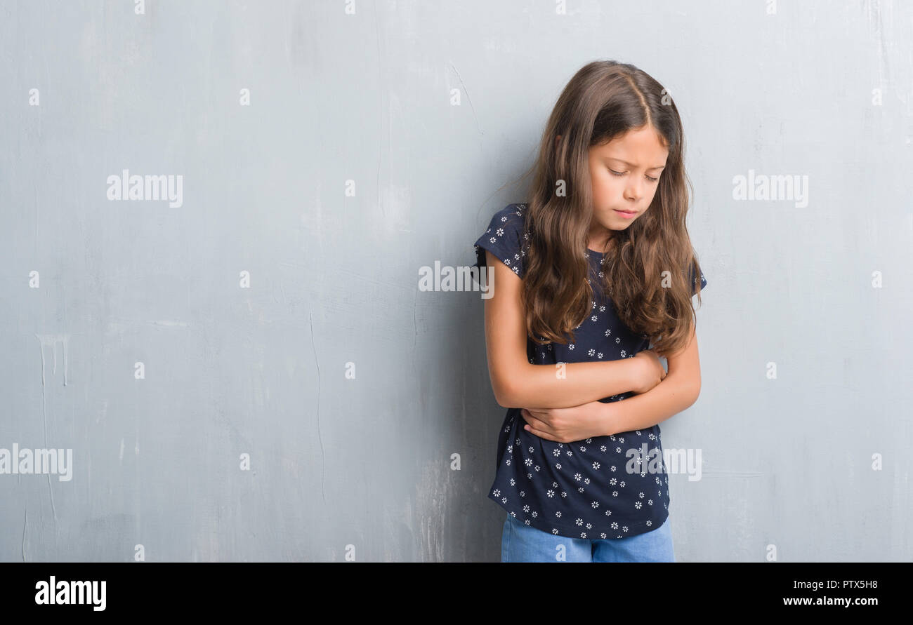 Young hispanic kid over grunge grey wall with hand on stomach because ...