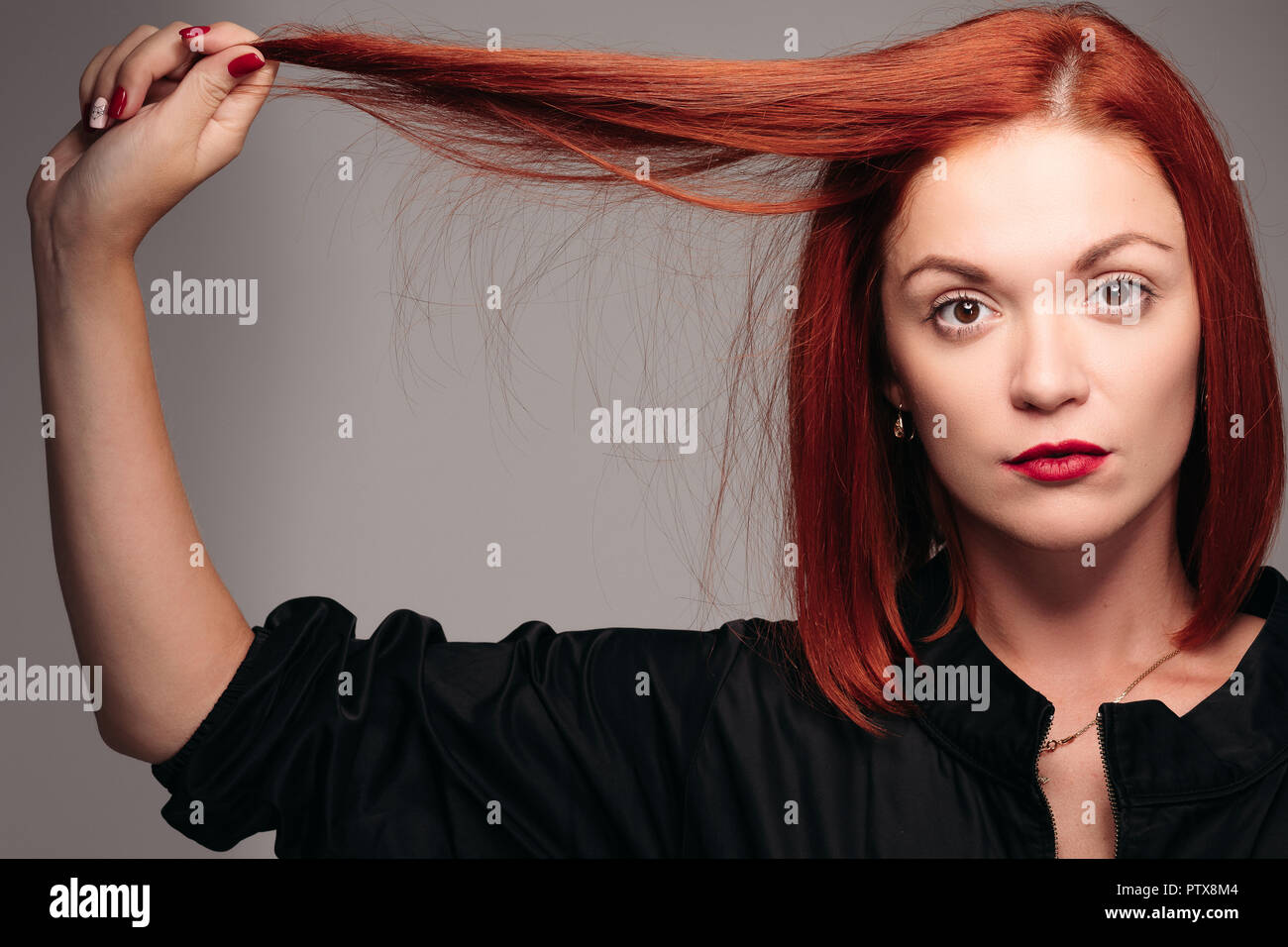 Serious girl with ginger hair holding lock of hair in hand Stock Photo ...