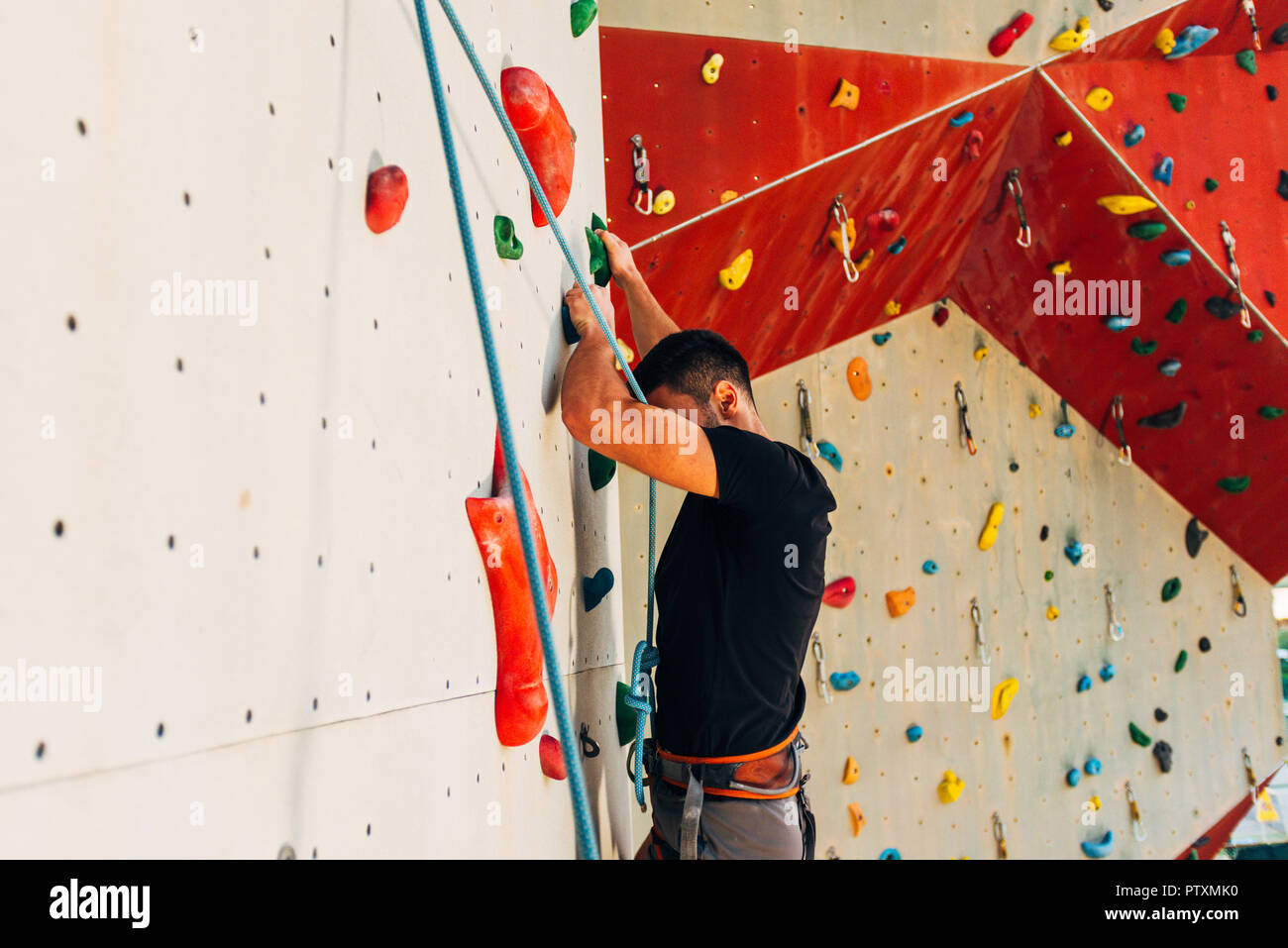 Man wearing belaying rope, climbing on a very high rock climbing wall ...