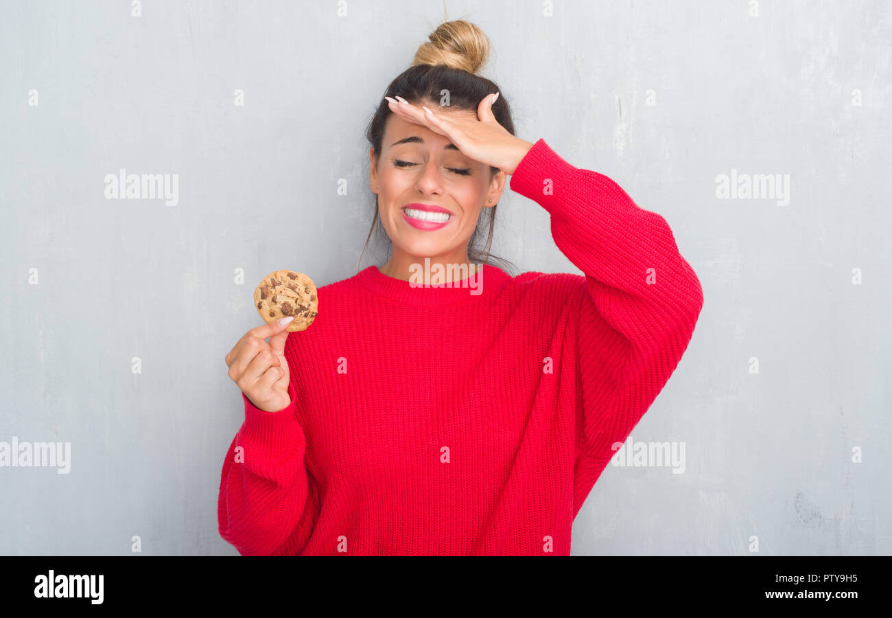 Young adult woman over grey grunge wall eating chocolate chip cooky ...