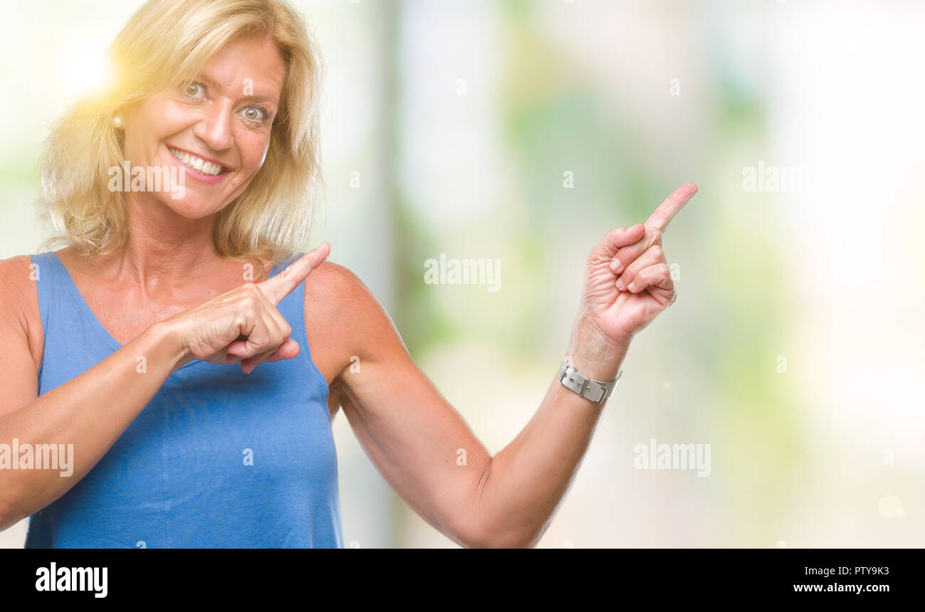 Middle age blonde woman over isolated background smiling and looking at the camera pointing with ...