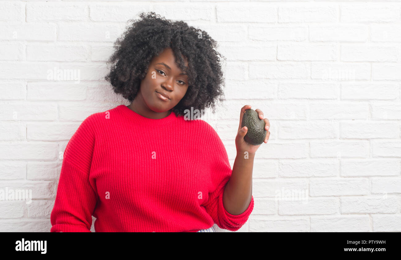 Young african american woman over white brick wall eating avocado with ...