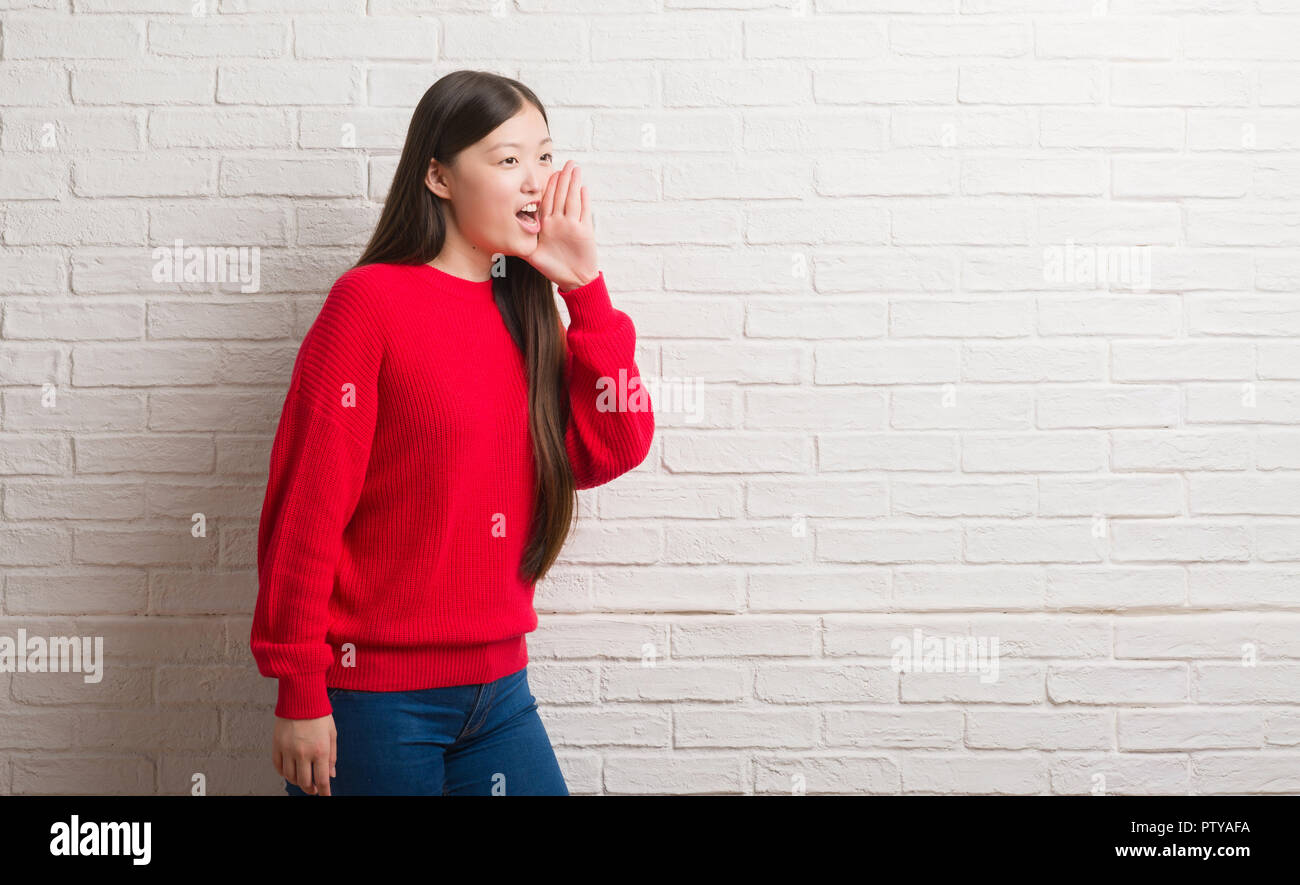 Young Chinese woman over brick wall shouting and screaming loud to side ...
