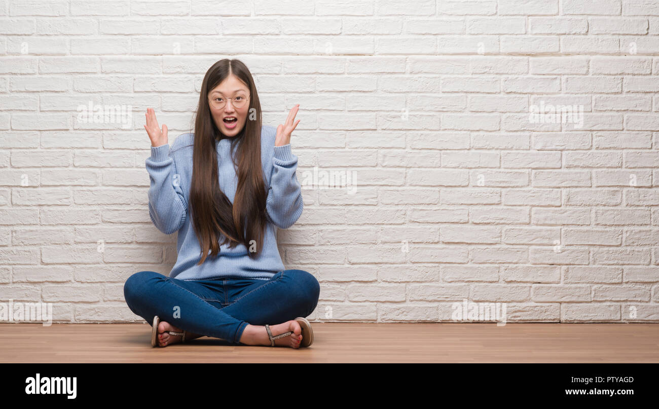 Young Chinese woman sitting on the floor over brick wall celebrating ...