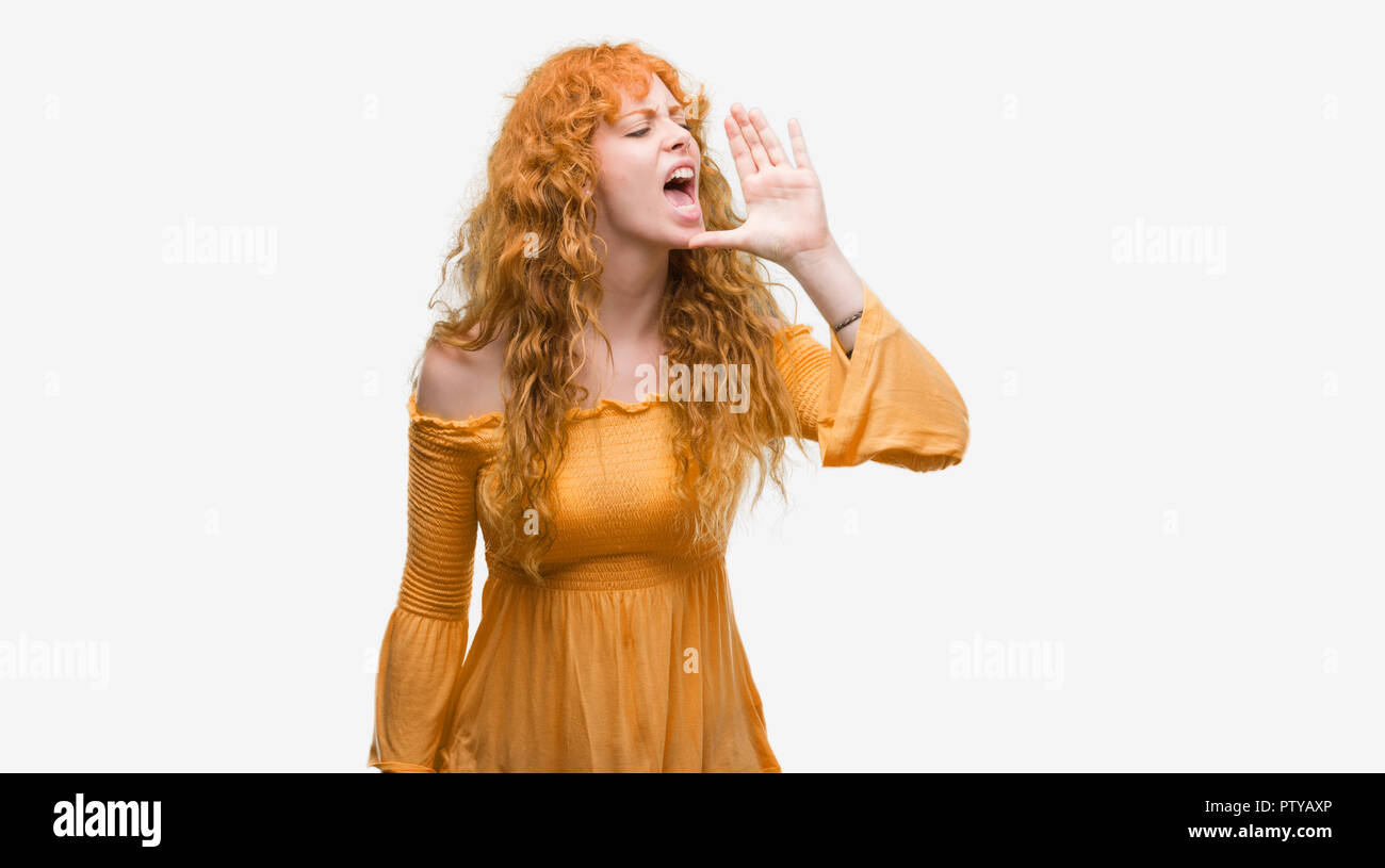 Young redhead woman shouting and screaming loud to side with hand on ...