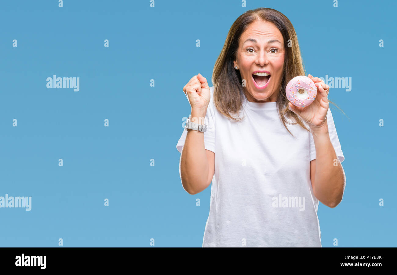 Middle age hispanic woman eating pink donut over isolated background ...