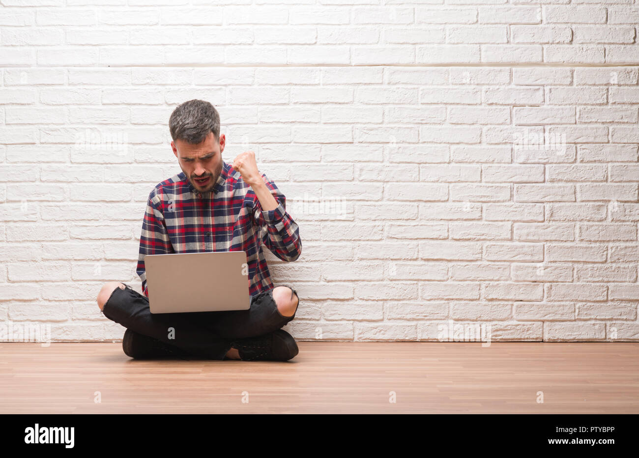 Young adult man over brick wall using laptop annoyed and frustrated ...