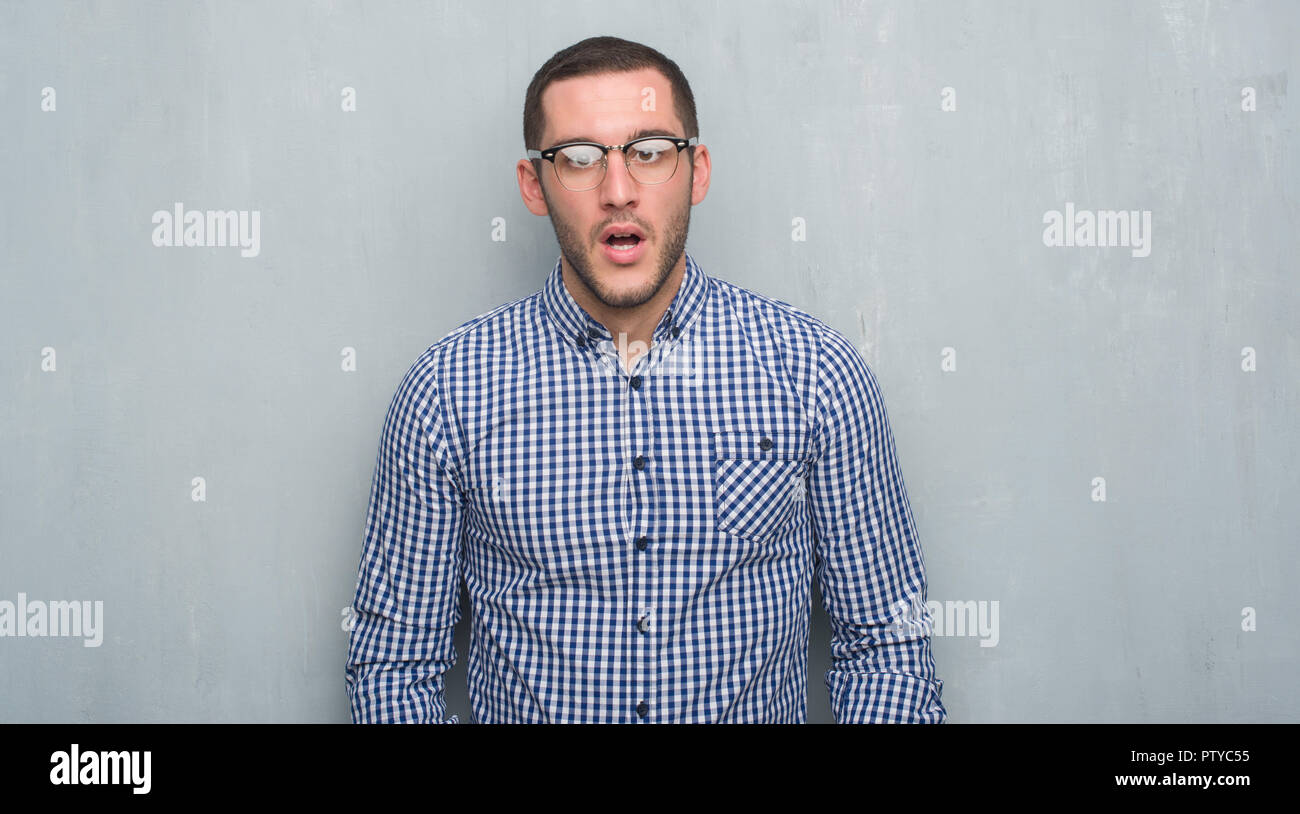 Young caucasian business man over grey grunge wall scared in shock with ...