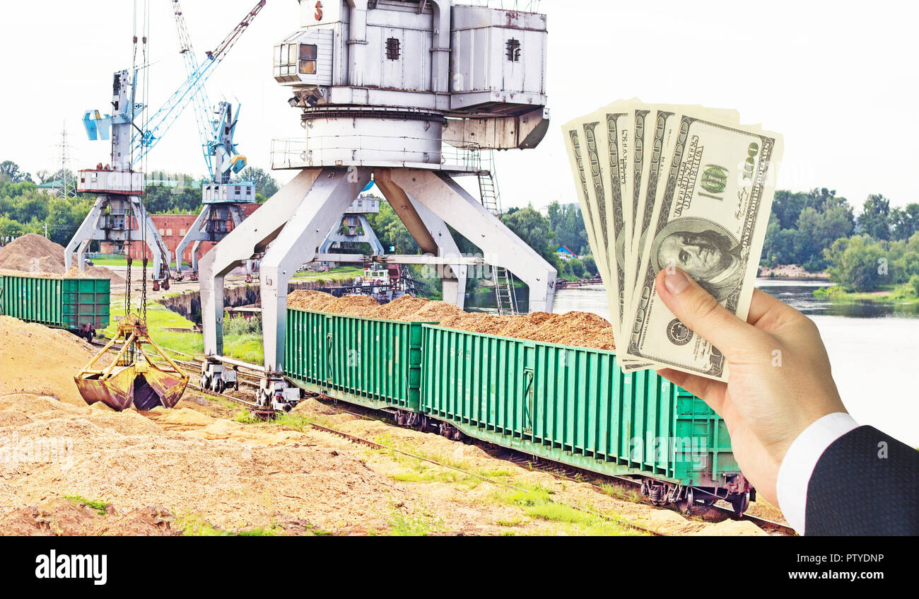 Hand with money dollars on the background of a port crane produces the ...