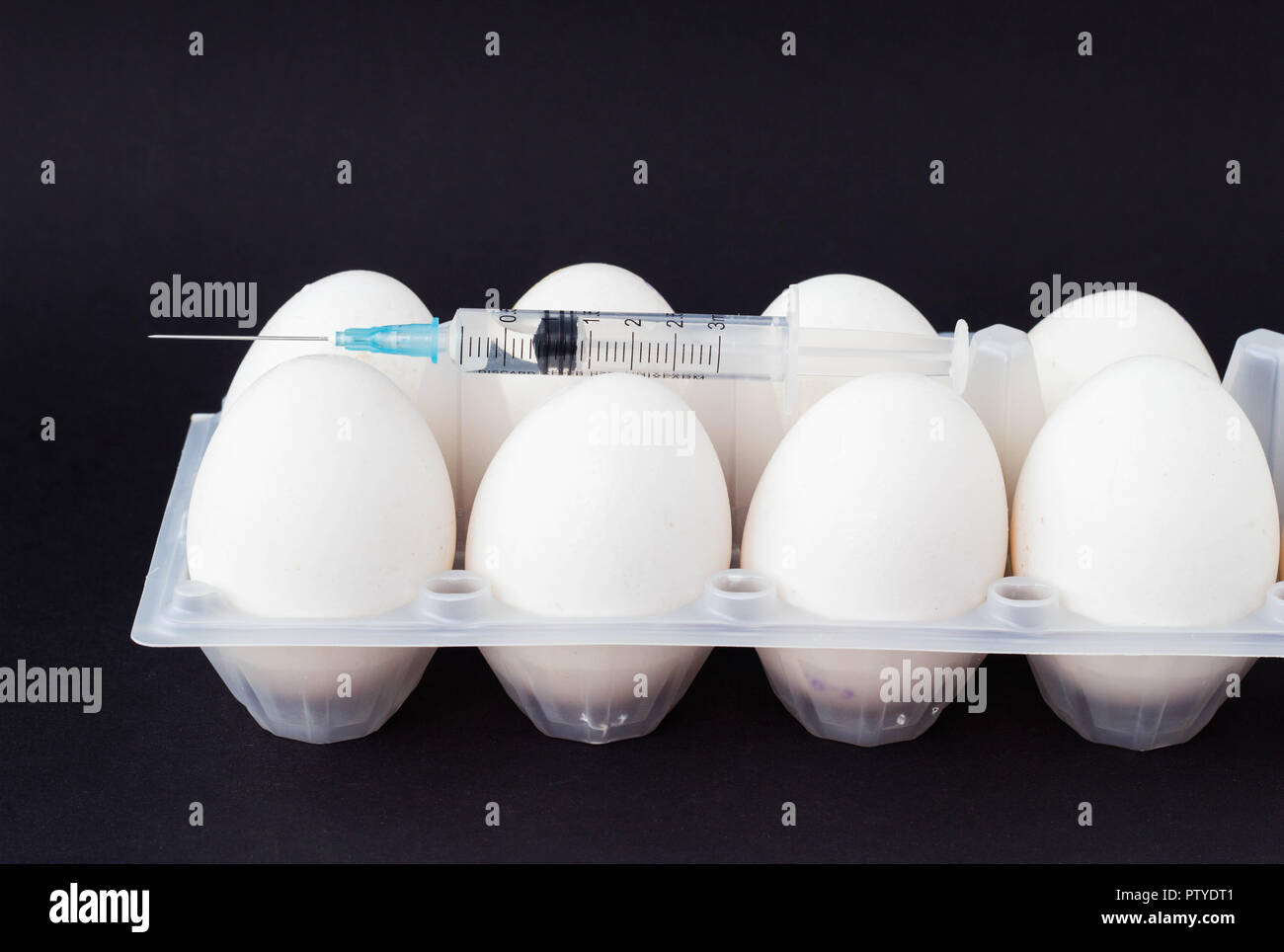 In an egg on a black background, a syringe is injected with a hormone ...