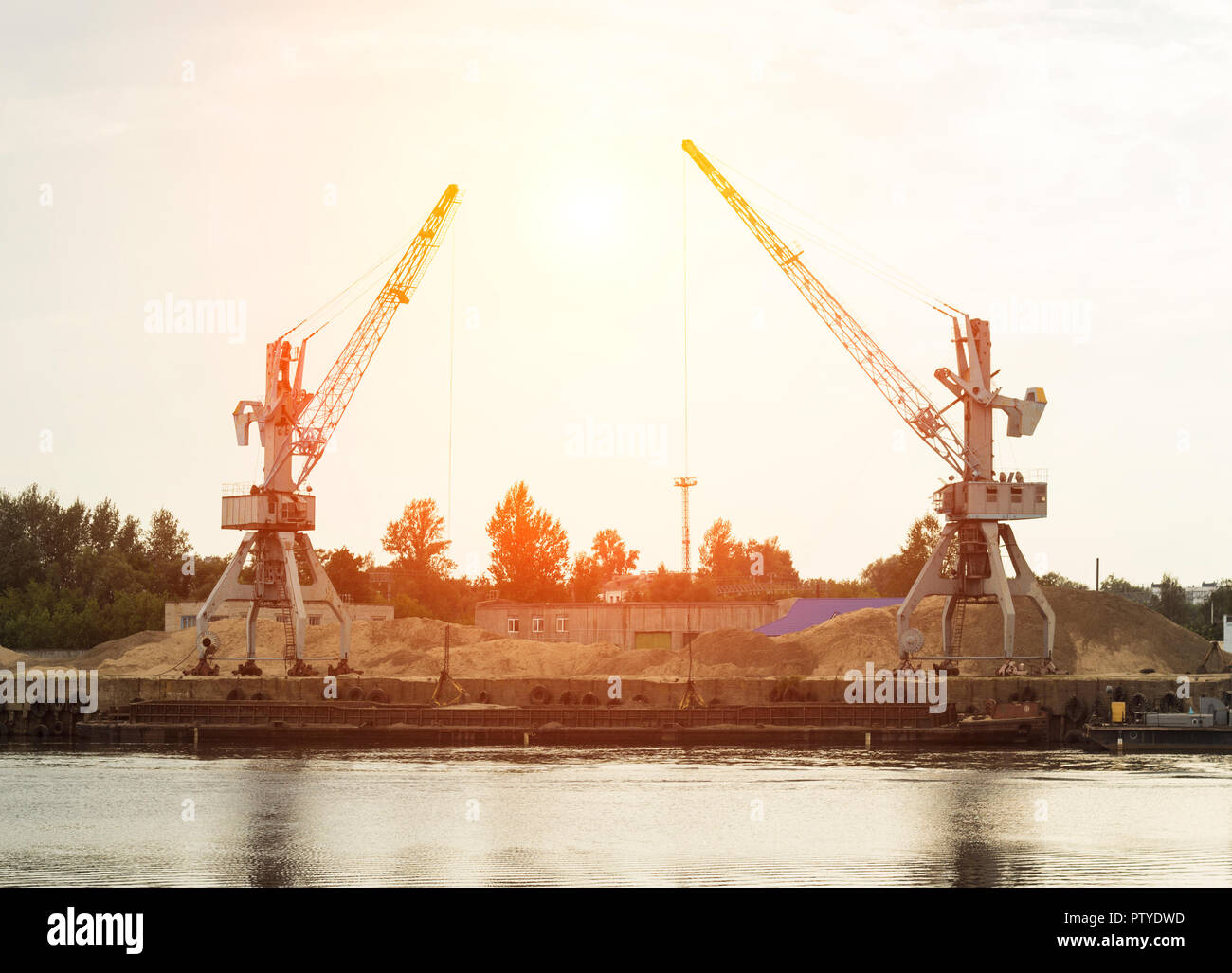 Two port cranes at the riverbank produce river sand, sunset, barge ...