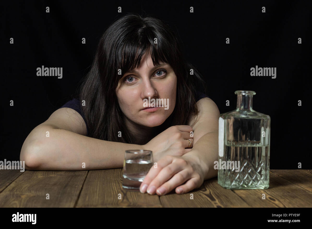 Girl at the table with alcohol in hands, black background, looks at the ...
