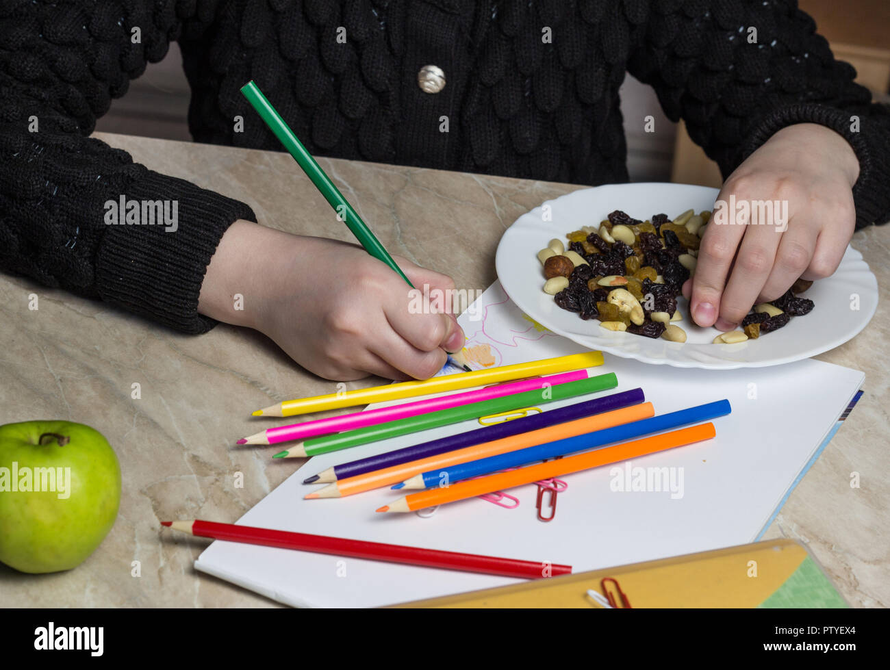 Girl doing homework and eating dried fruits Stock Photo - Alamy