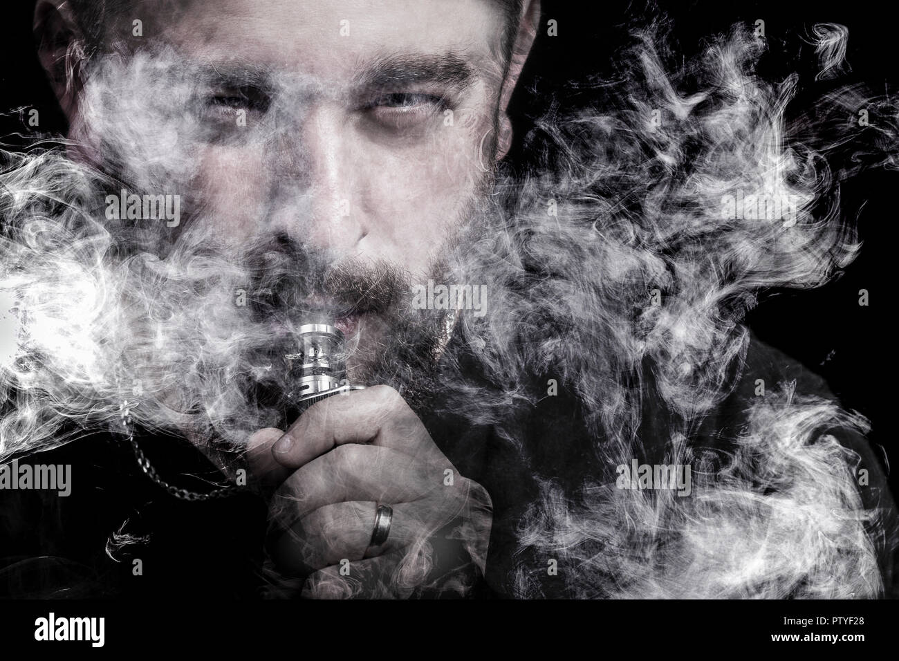 man on black background close-up with vape in mouth surrounded by smoke ...