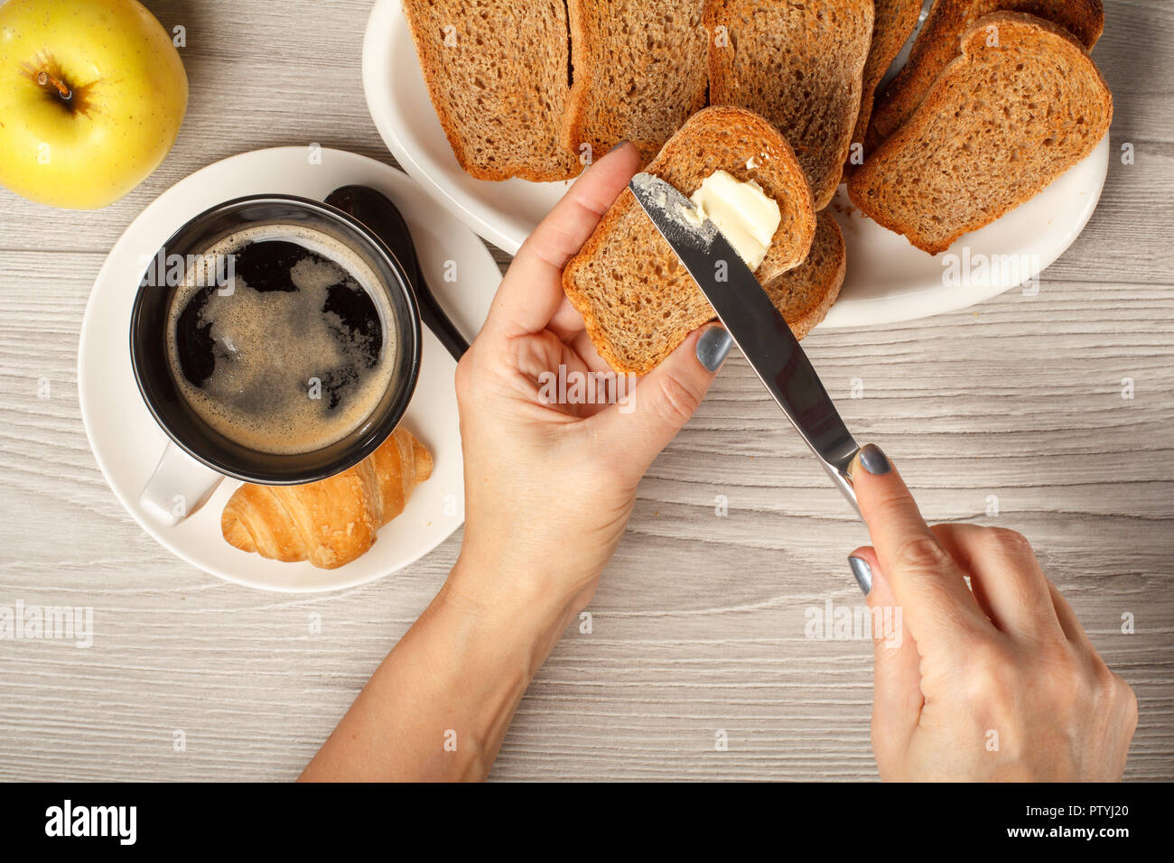 Top view of female hands spreading butter on toast at the table with ...
