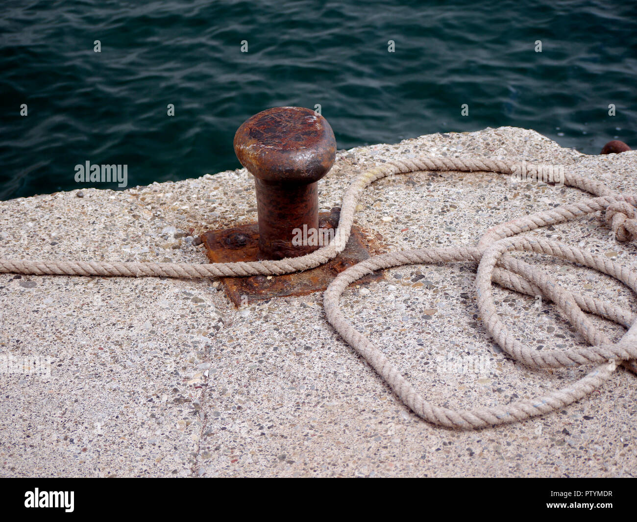 Mooring post on harbour wall with rope alongside Stock Photo - Alamy