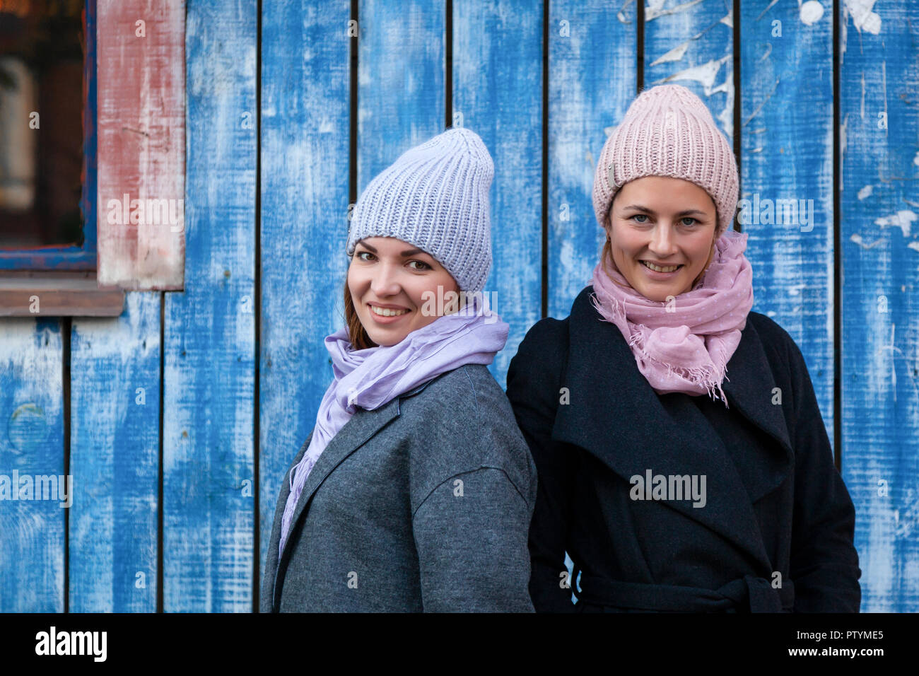 Two cheerful girlfriends are smiling and posing against the bright blue ...