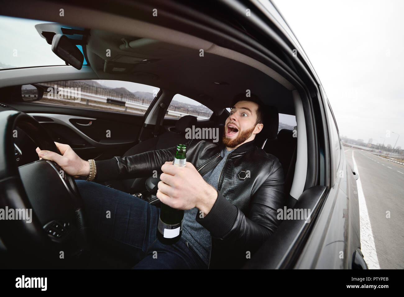 Drunk young man with a beard with a bottle of beer in his hand behind ...