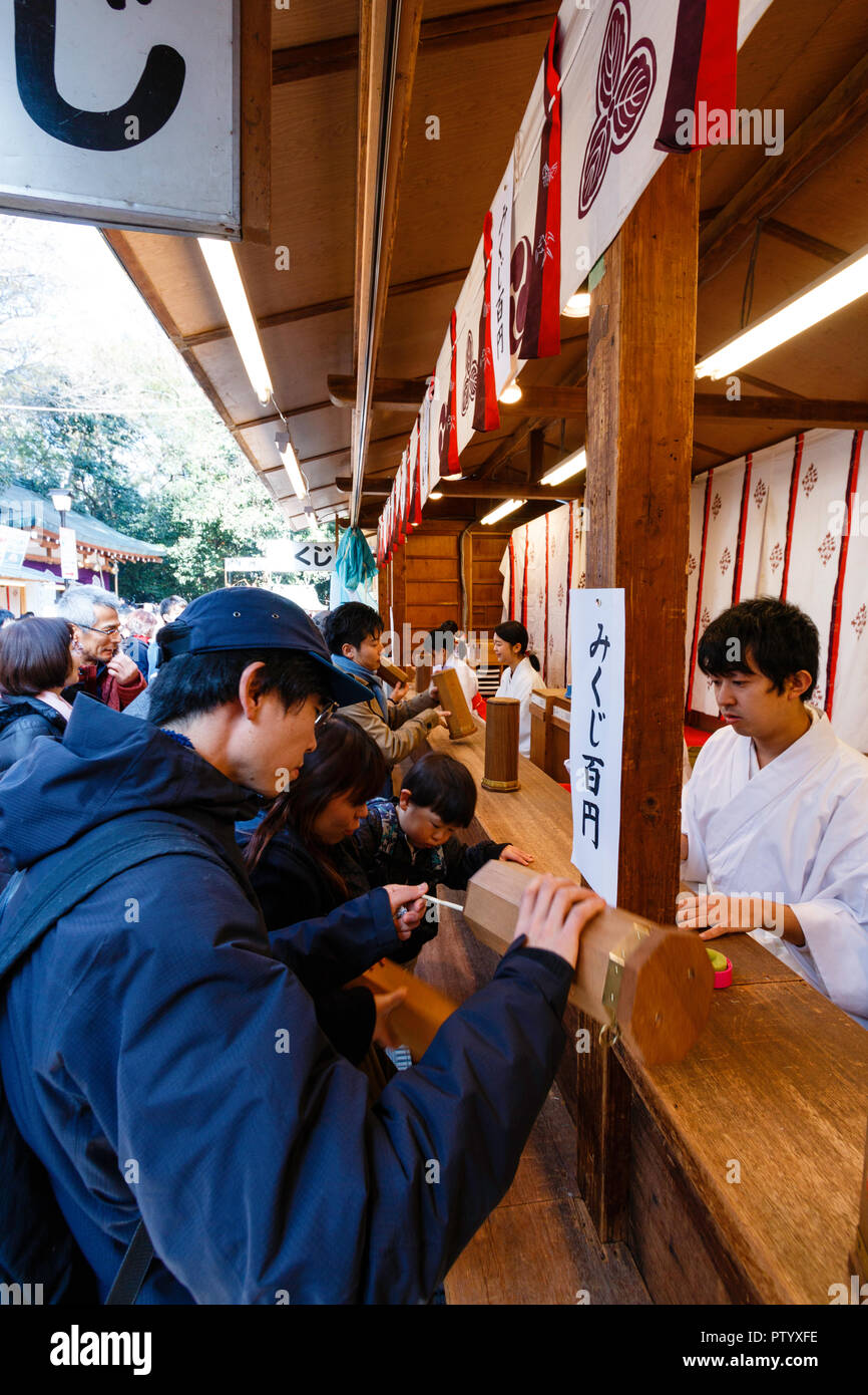 Japanese new year, shogatsu. Shrine Maidens, Miko, at busy counter selling Omikuji paper fortune ...
