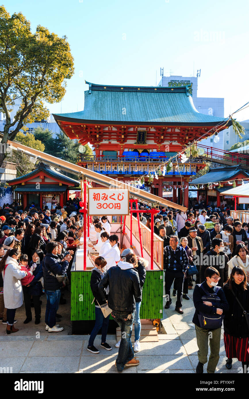 Japanese new year, shogatsu. Shrine Maidens, Miko, at busy counter selling Omikuji paper fortune ...