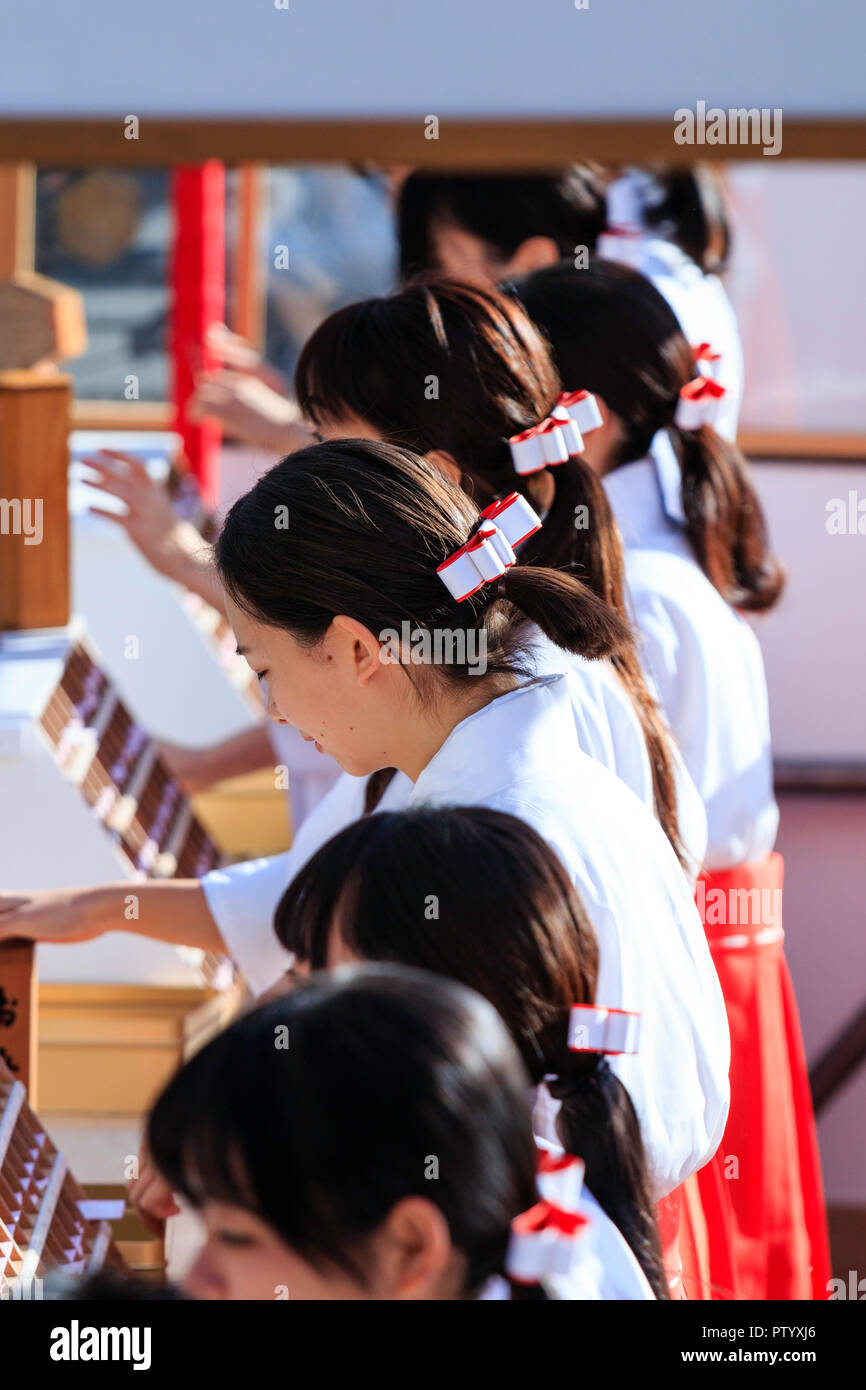 Japanese new year, shogatsu. Shrine Maidens, Miko, at busy counter selling Omikuji paper fortune ...